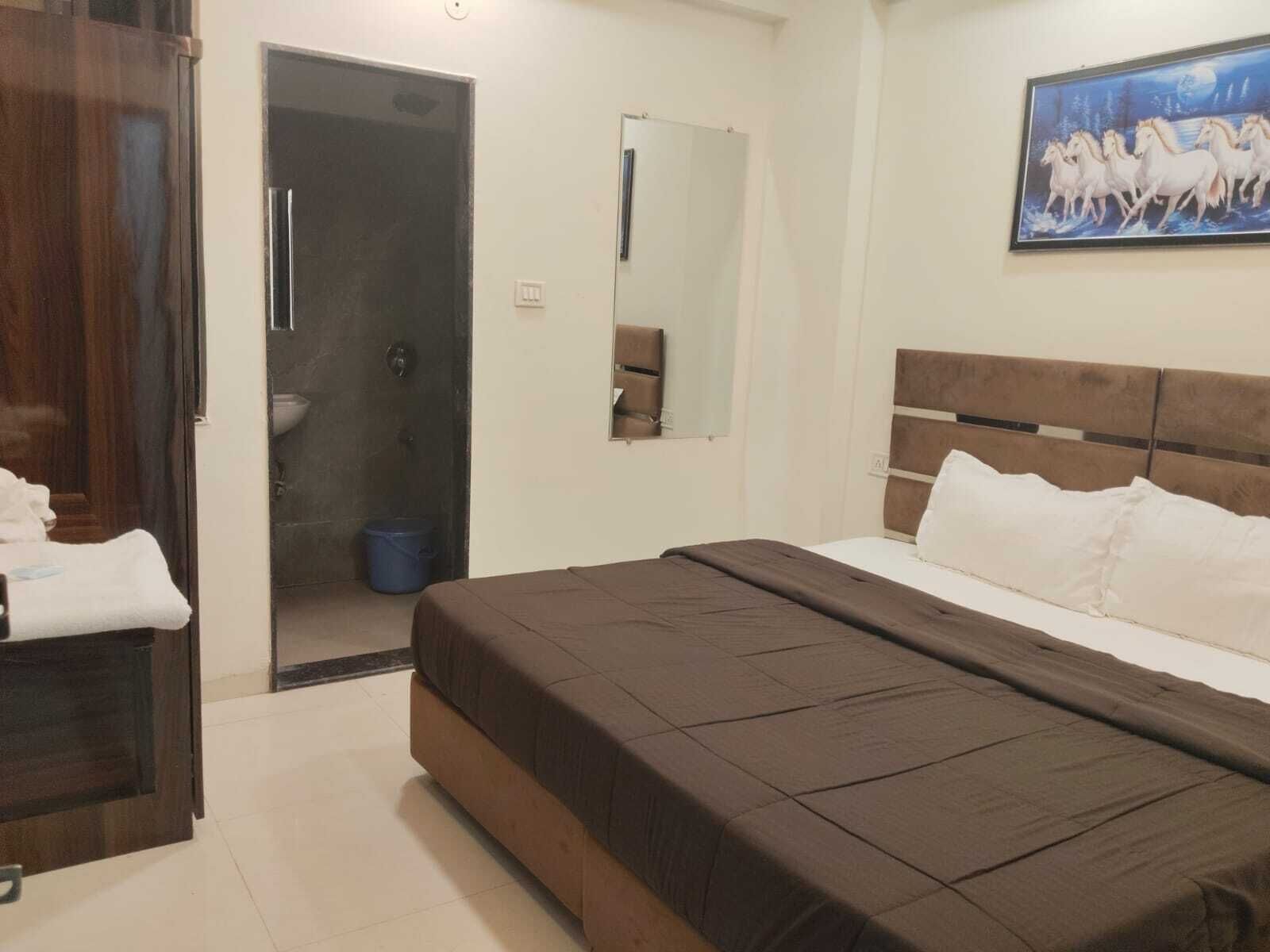 Quarto com uma cama grande, um guarda-roupa de madeira, banheiro com espelho e um quadro na parede.