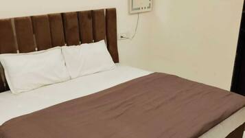 Cama bem arrumada com colcha marrom e almofadas brancas, cabeceira de madeira e luminária fixada na parede.