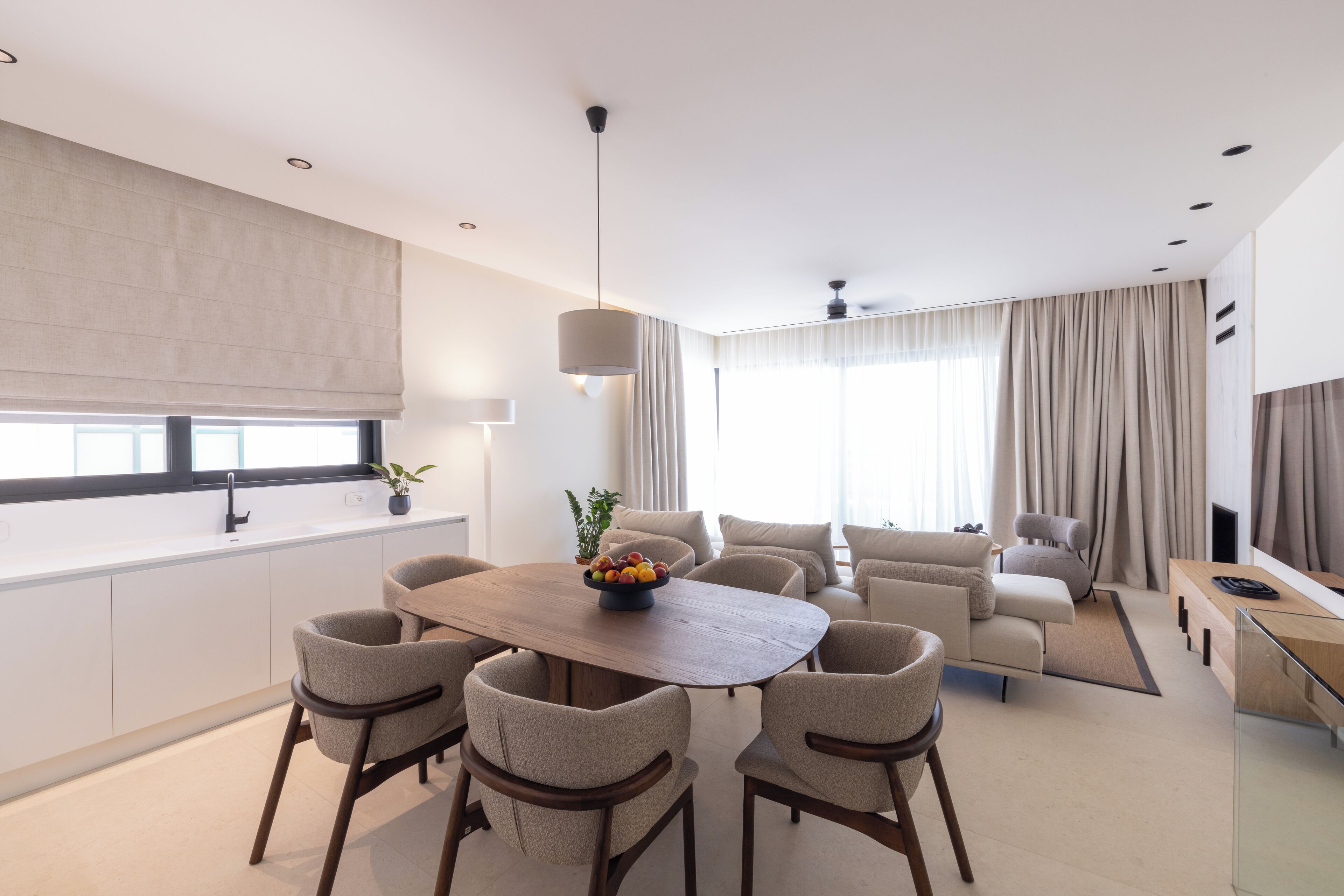 Sala de estar moderna com mesa de jantar de madeira, sofás bege e uma grande janela com cortinas.