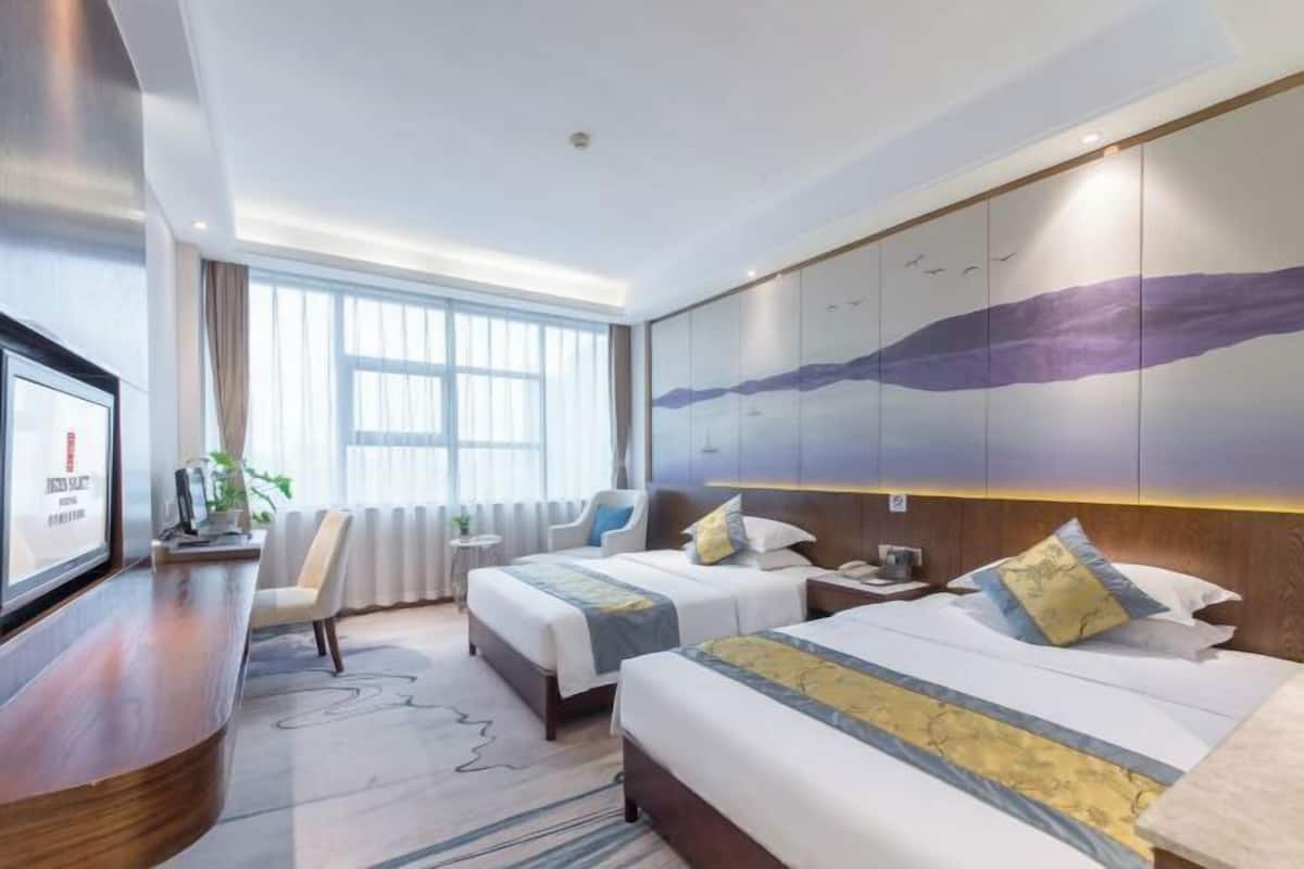 Quarto de hotel com duas camas, televisão, escrivaninha e uma janela grande.