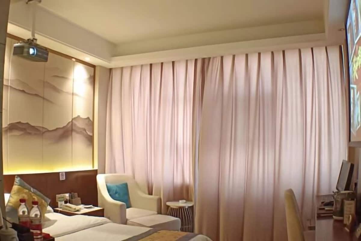 Quarto de hotel com duas camas, área de estar, uma mesinha e um projetor.