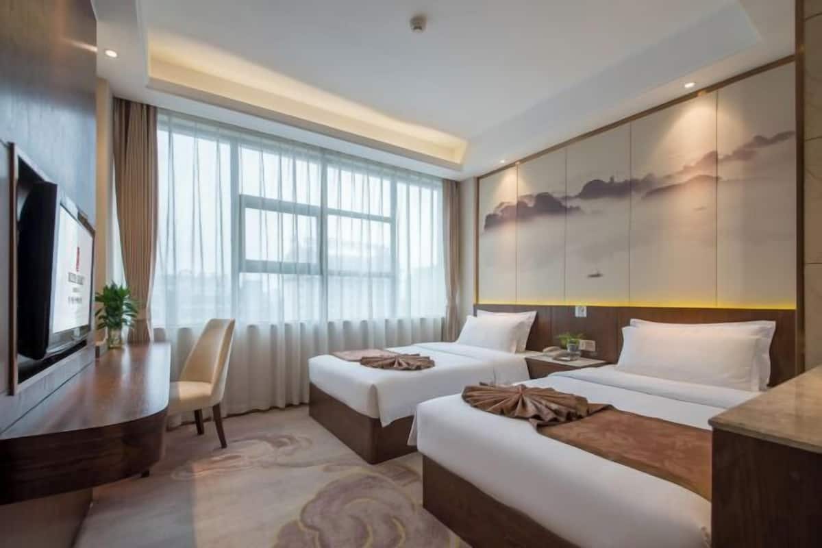 Quarto de hotel com duas camas, televisão, escrivaninha, cadeira e uma janela grande.