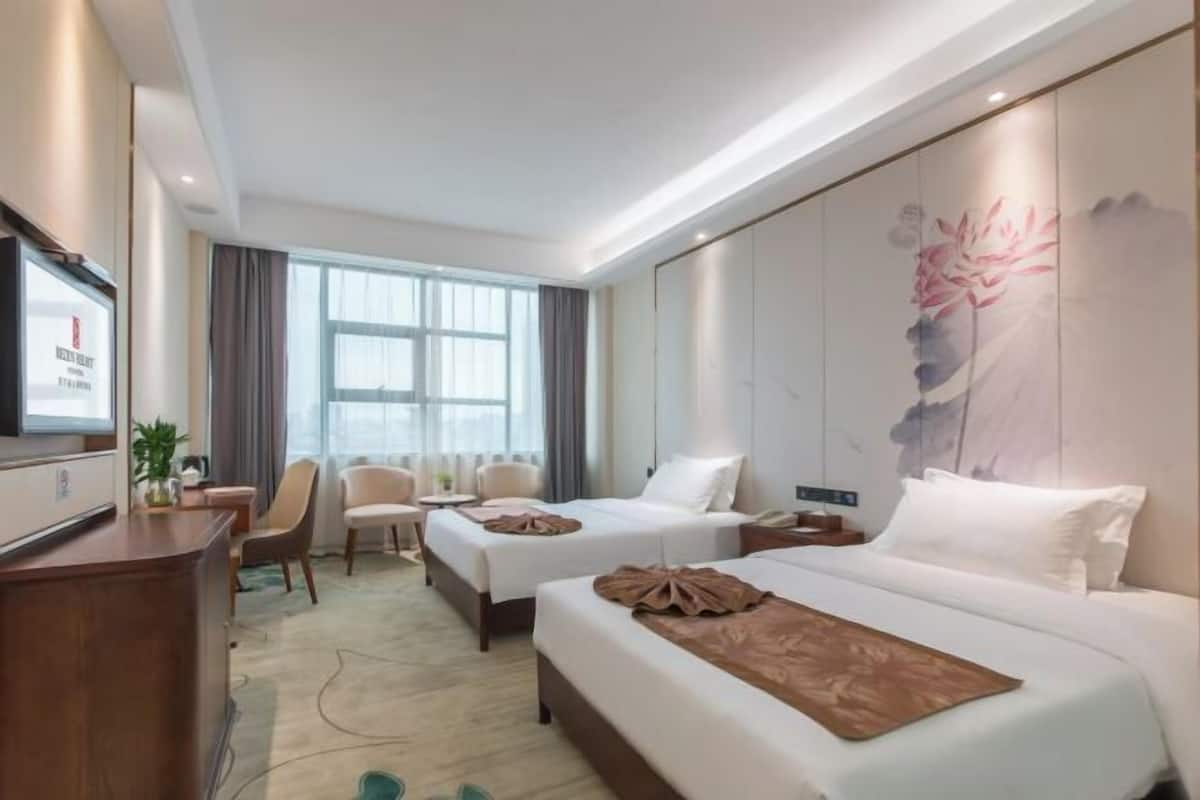 Quarto de hotel com duas camas, uma escrivaninha, televisão e uma janela grande.