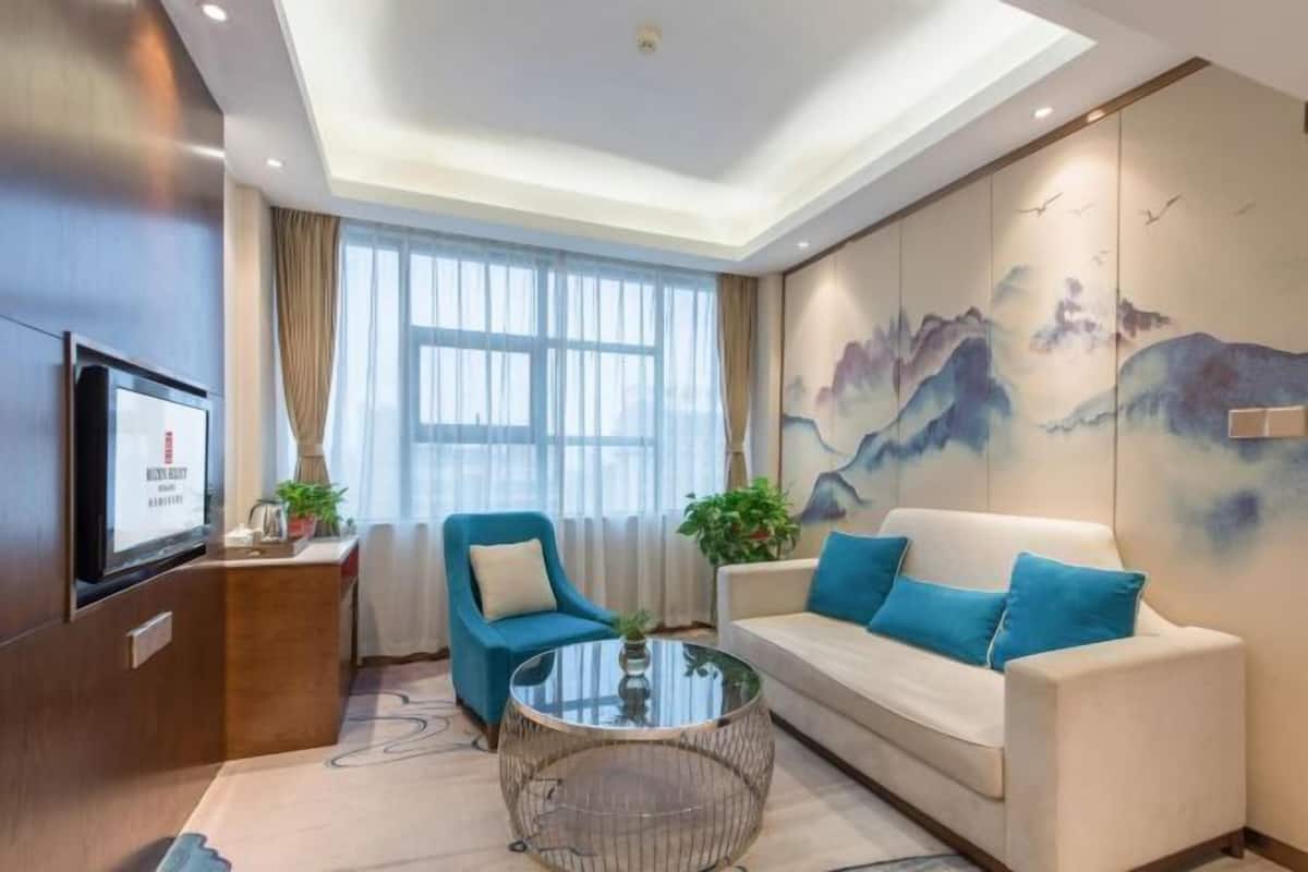 Uma sala de estar moderna com um sofá, poltrona e mesa de centro. Há uma televisão à esquerda e um quadro na parede.