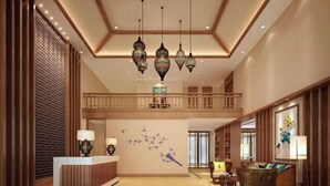 Um hall amplo com teto alto, painéis de madeira e um lustre central.