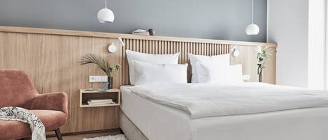 Quarto moderno com cabeceira de madeira, cama branca, poltrona rosa e tapete branco.