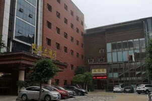 Edifício com fachada de tijolos vermelhos, entrada de vidro moderna e vários carros estacionados.