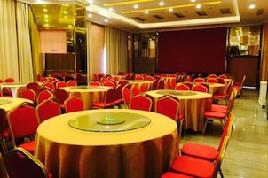Salão de banquetes com mesas redondas e cadeiras vermelhas, palco e área de bar.