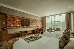 Quarto de hotel com parede em padrão de tijolos, televisão de tela plana, cama com colcha estampada, escrivaninha com abajur e uma grande janela com cortinas.