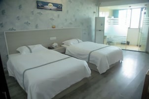 Quarto de hotel com duas camas, uma mesa de cabeceira, um relógio na parede e uma porta que dá para o banheiro.
