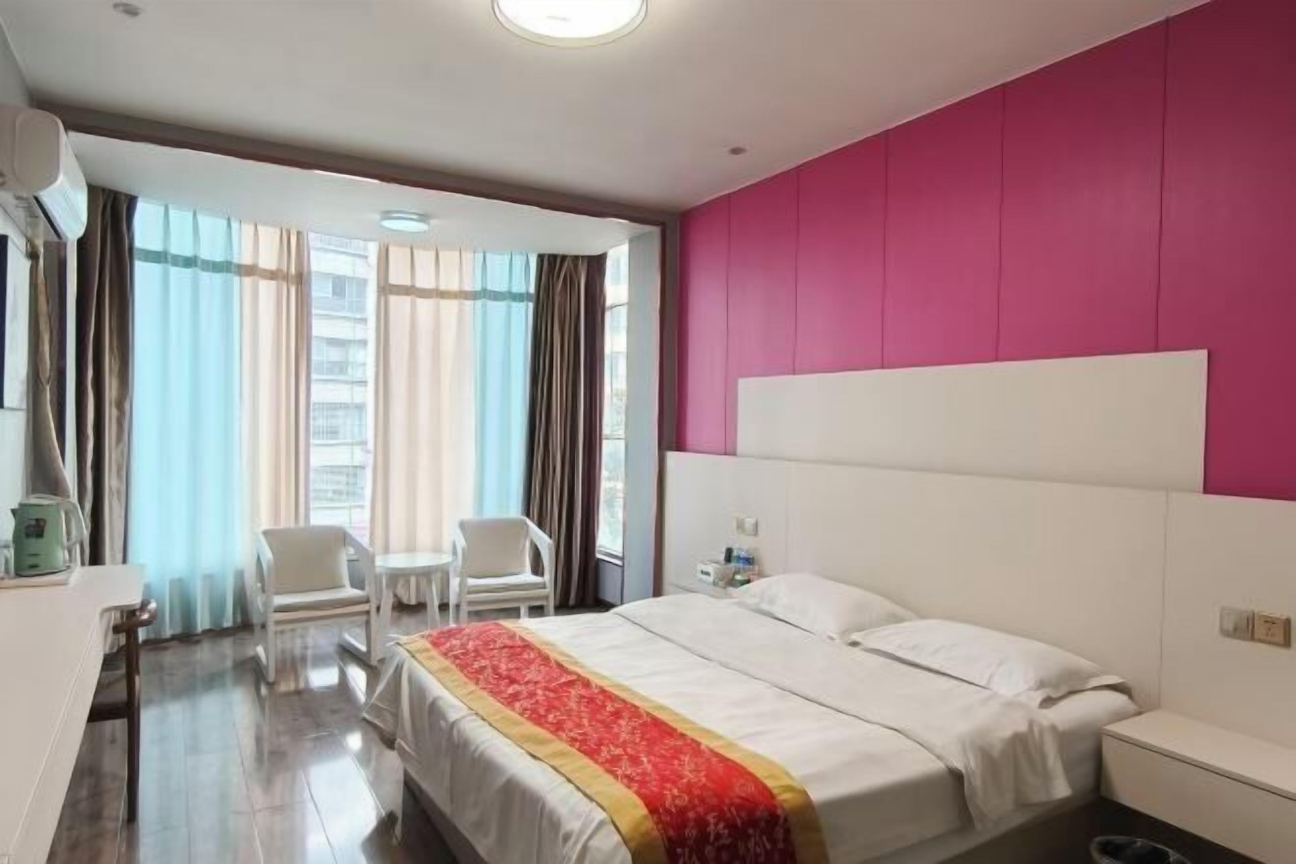 Quarto de hotel com uma cama grande, uma escrivaninha, uma cadeira e uma janela com cortinas.