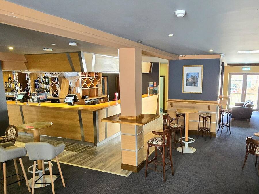 Um restaurante com área de bar, diversas opções de assentos incluindo banquetas e mesas, e um balcão com caixa registradora.