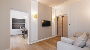 Uma sala de estar moderna com sofá, televisão de tela plana na parede e área de cozinha com mesa e cadeiras.