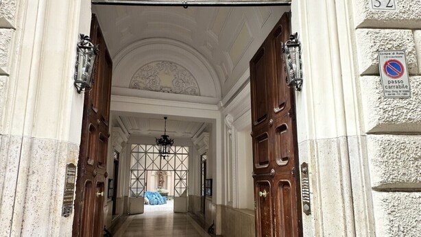 Uma entrada imponente com piso de azulejos, portas de madeira ornamentadas e teto decorativo.