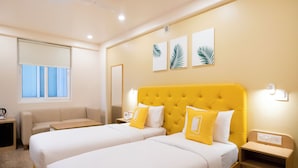 Quarto de hotel com duas camas, um sofá, uma mesinha e uma janela com persianas.