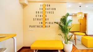 Um quarto com piso de madeira, um banco amarelo, uma planta em vaso e uma parede com palavras motivacionais.