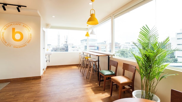 Um café moderno com piso de madeira, luminárias pendentes amarelas e uma grande janela com vista para a cidade.