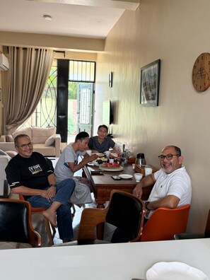 Um grupo de pessoas jantando em um ambiente com mesa, cadeiras e um sofá.