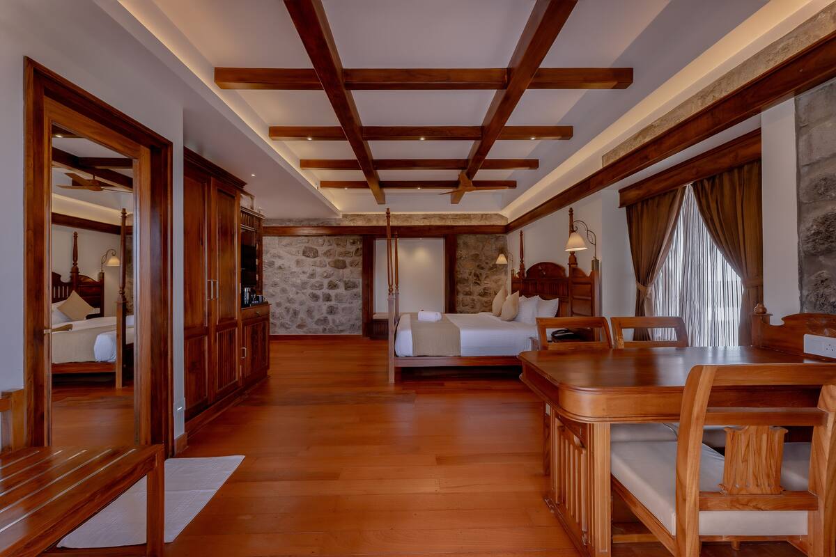 Um quarto amplo com piso de madeira, uma cama grande, uma mesa de jantar e uma parede de pedra.