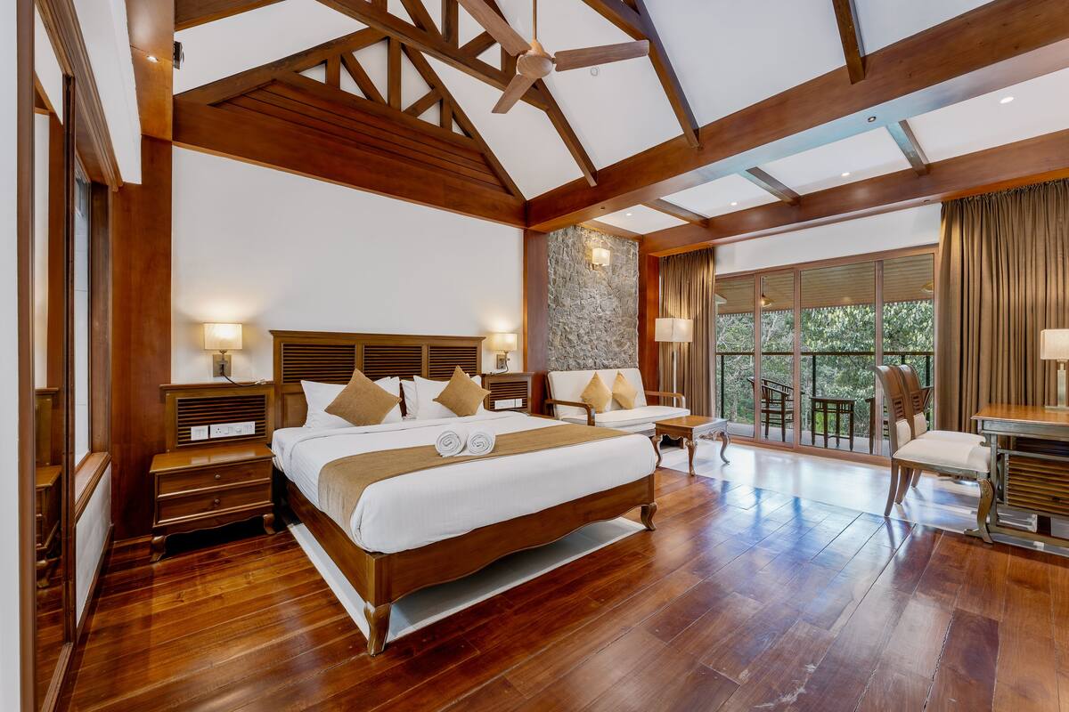 Um quarto espaçoso com uma cama grande, vigas de madeira, parede de destaque em pedra e vista para o exterior.