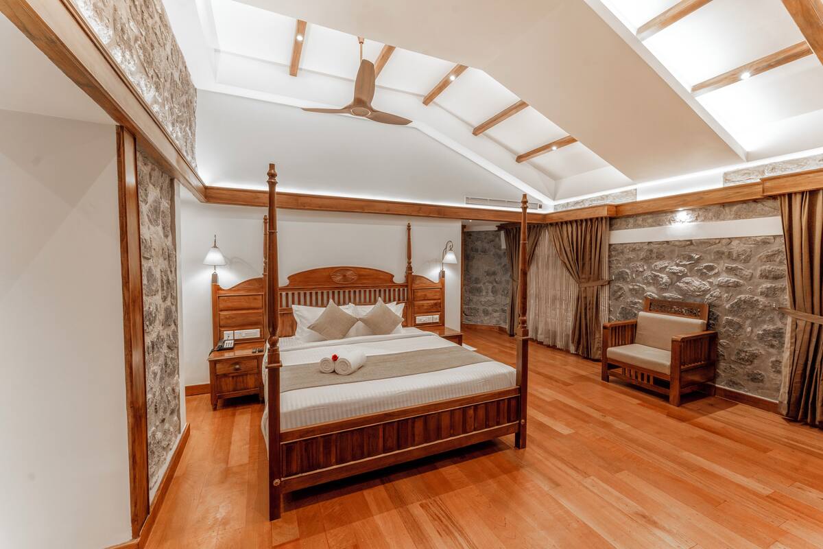 Uma cama de dossel com cabeceira de madeira, mesa de cabeceira, mesinha de apoio e uma cadeira.