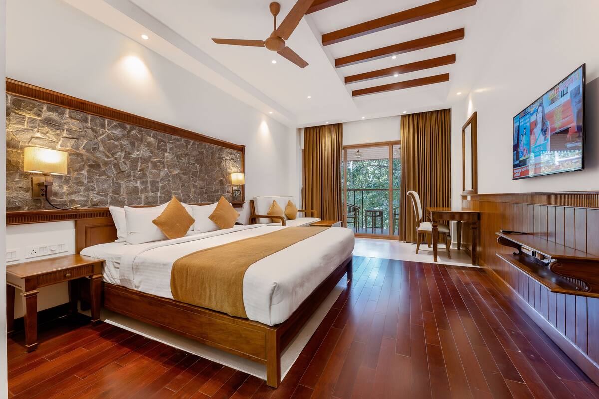 Quarto de hotel moderno com uma cama grande, cabeceira de madeira, parede de destaque em pedra e televisão na parede.