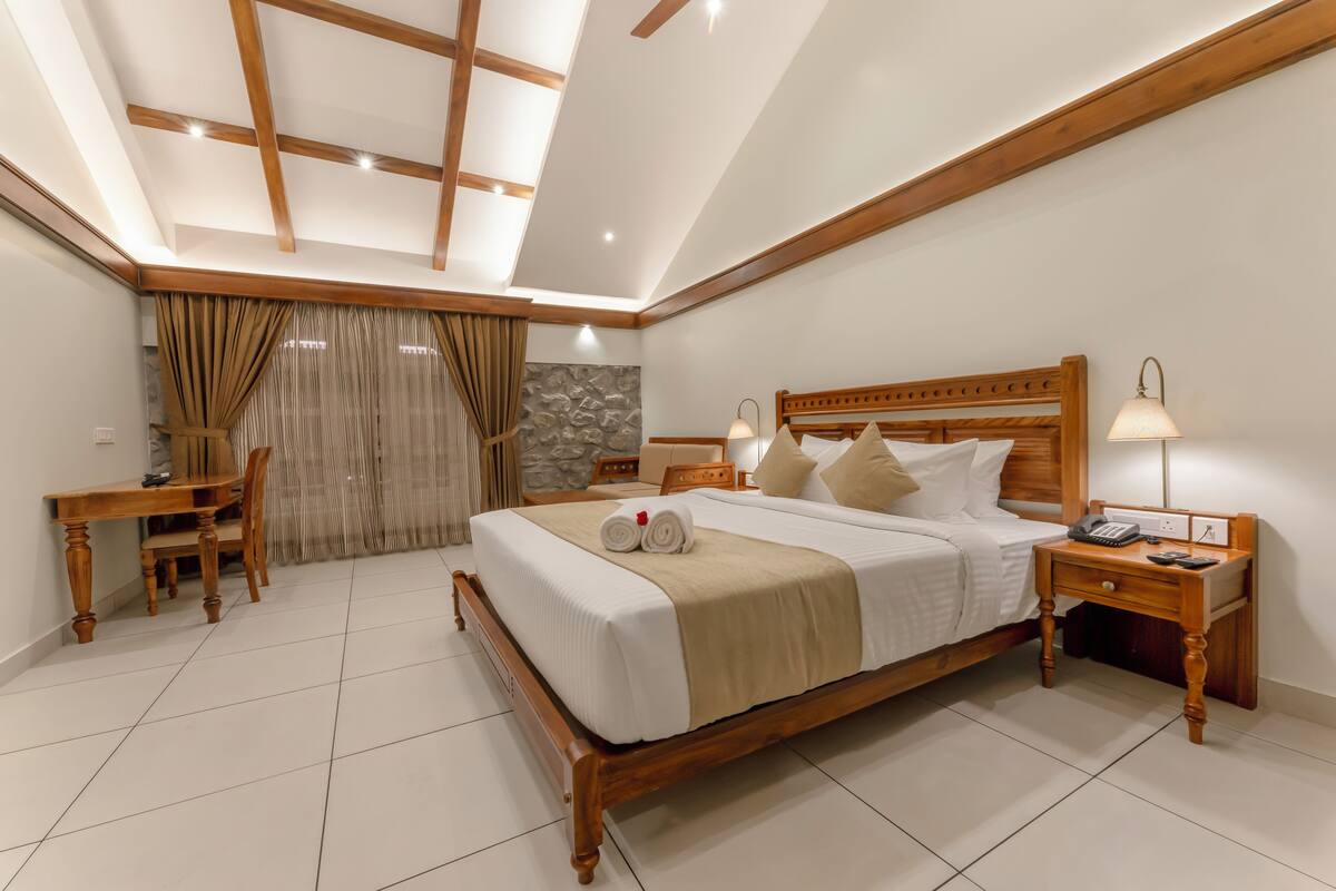Quarto moderno com uma cama grande, cabeceira de madeira, mesas de cabeceira com luminárias, uma escrivaninha e uma cadeira.