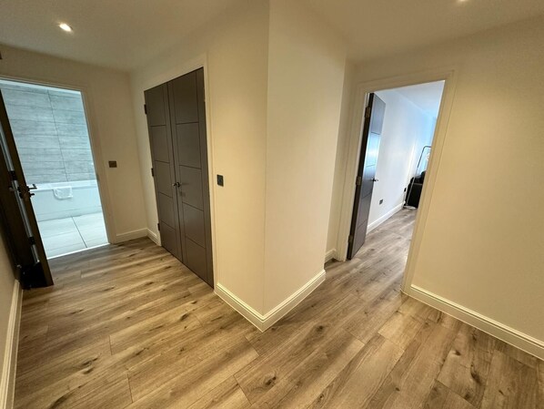 Corredor com piso de madeira, porta deslizante e vista para outro quarto.