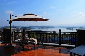 Um terraço com vista para a água, uma mesa, cadeiras e um guarda-sol.