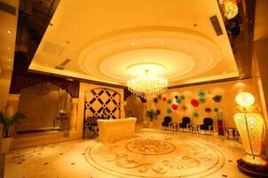 Um saguão de hotel com um lustre imponente, um carpete estampado e uma mesa de recepção.