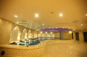 Uma grande piscina interior com design curvo, rodeada por um teto alto com iluminação embutida.