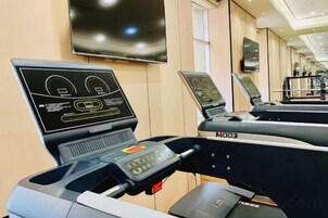 Uma academia com esteiras e equipamentos de ginástica, uma televisão fixada na parede e uma janela que oferece luz natural.