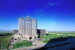 Um hotel moderno com vários andares e um pátio central, rodeado por vegetação e um céu límpido.