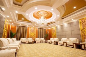 Sala de conferência com mesa redonda, várias cadeiras, um candelabro e padrões decorativos nas paredes.