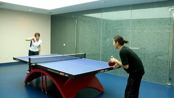 Uma mesa de ping pong em um espaço com divisória de vidro e piso azul.