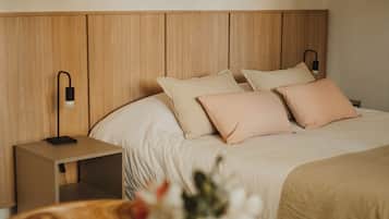 Uma cama bem arrumada com cabeceira de madeira, uma mesa de cabeceira com abajur e um criado-mudo pequeno.