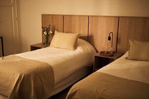 Quarto de hotel com duas camas, painel de cabeceira de madeira, mesas de cabeceira com abajures e um vaso com flores.