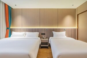 Quarto de hotel com duas camas, cabeceira de madeira, mesa de cabeceira com abajur e luminária na parede.