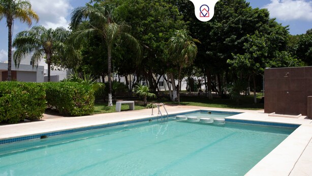 Piscina com borda azulejada, rodeada por palmeiras e vegetação, com céu claro acima.