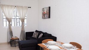 Uma sala de estar moderna com um sofá preto, uma mesa de jantar de madeira para quatro pessoas e uma pequena mesa lateral com um cesto.