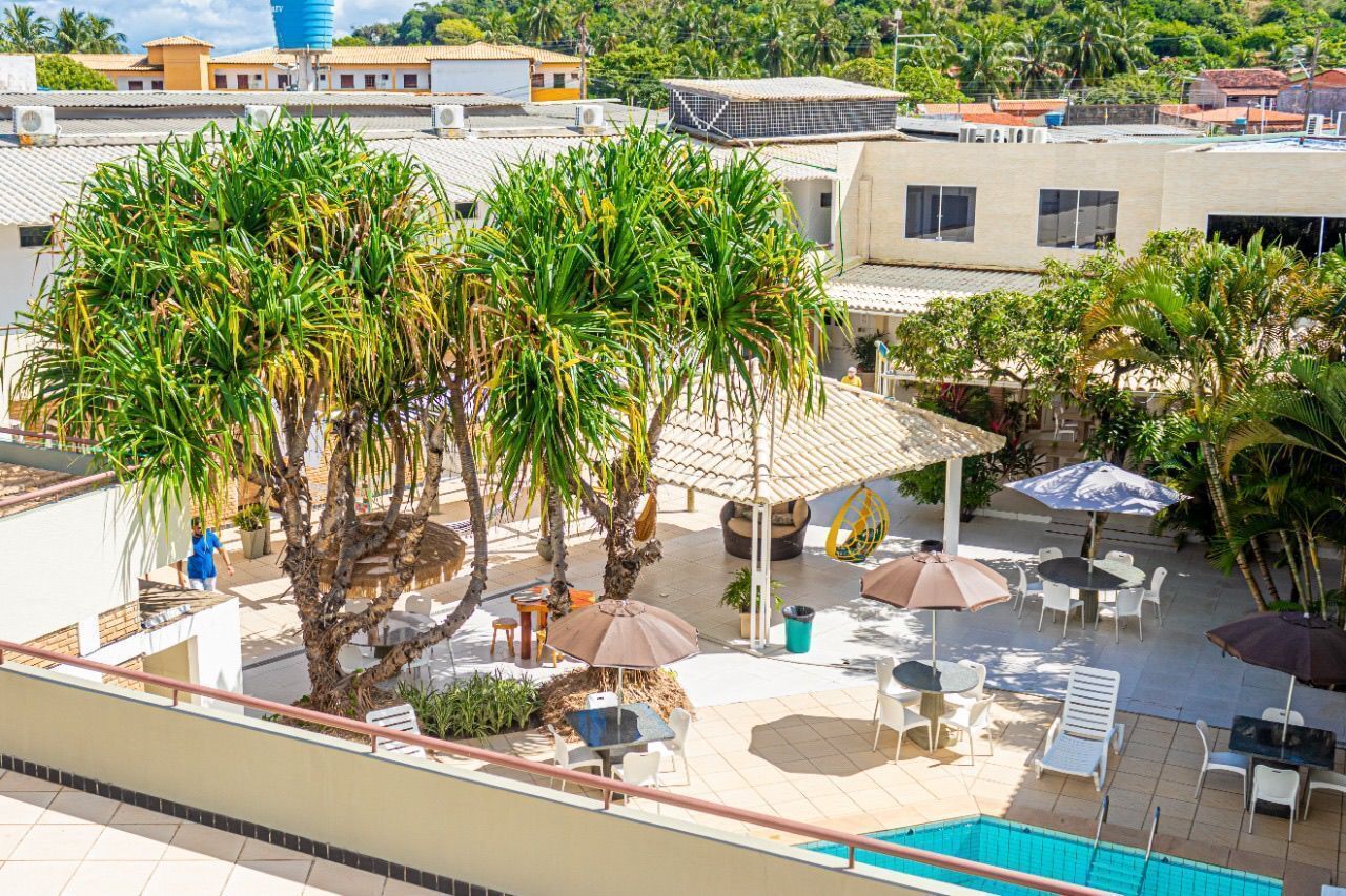 Área de piscina no terraço com espreguiçadeiras, guarda-sóis e palmeiras.