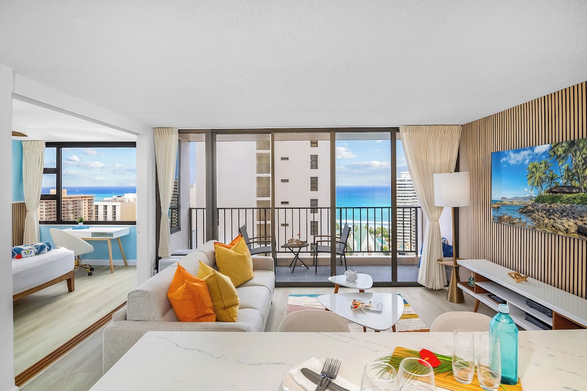 Quarto de hotel moderno com varanda, sofá, mesa de jantar e televisão.