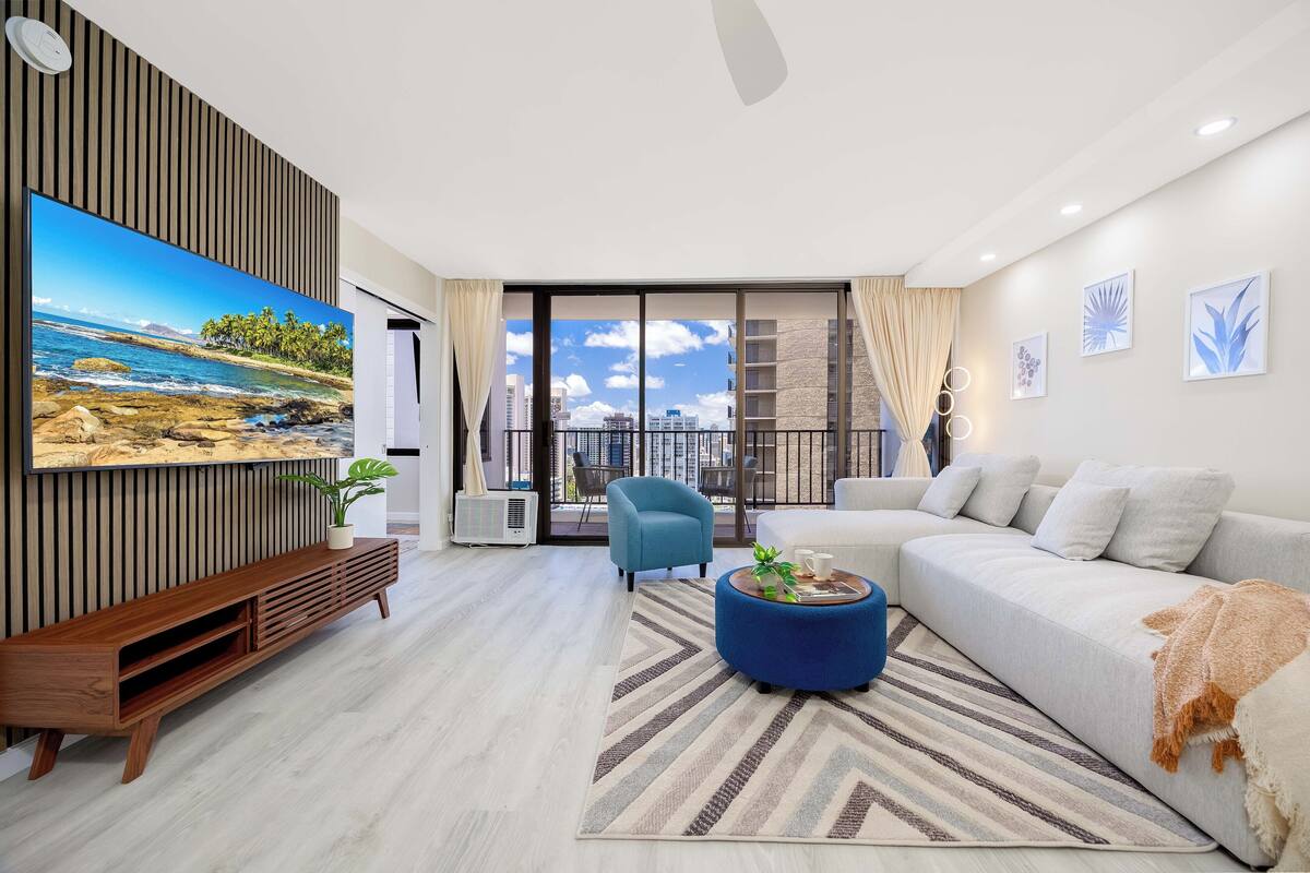 Uma sala de estar moderna com uma televisão grande, um sofá, uma poltrona azul e uma mesa de centro.