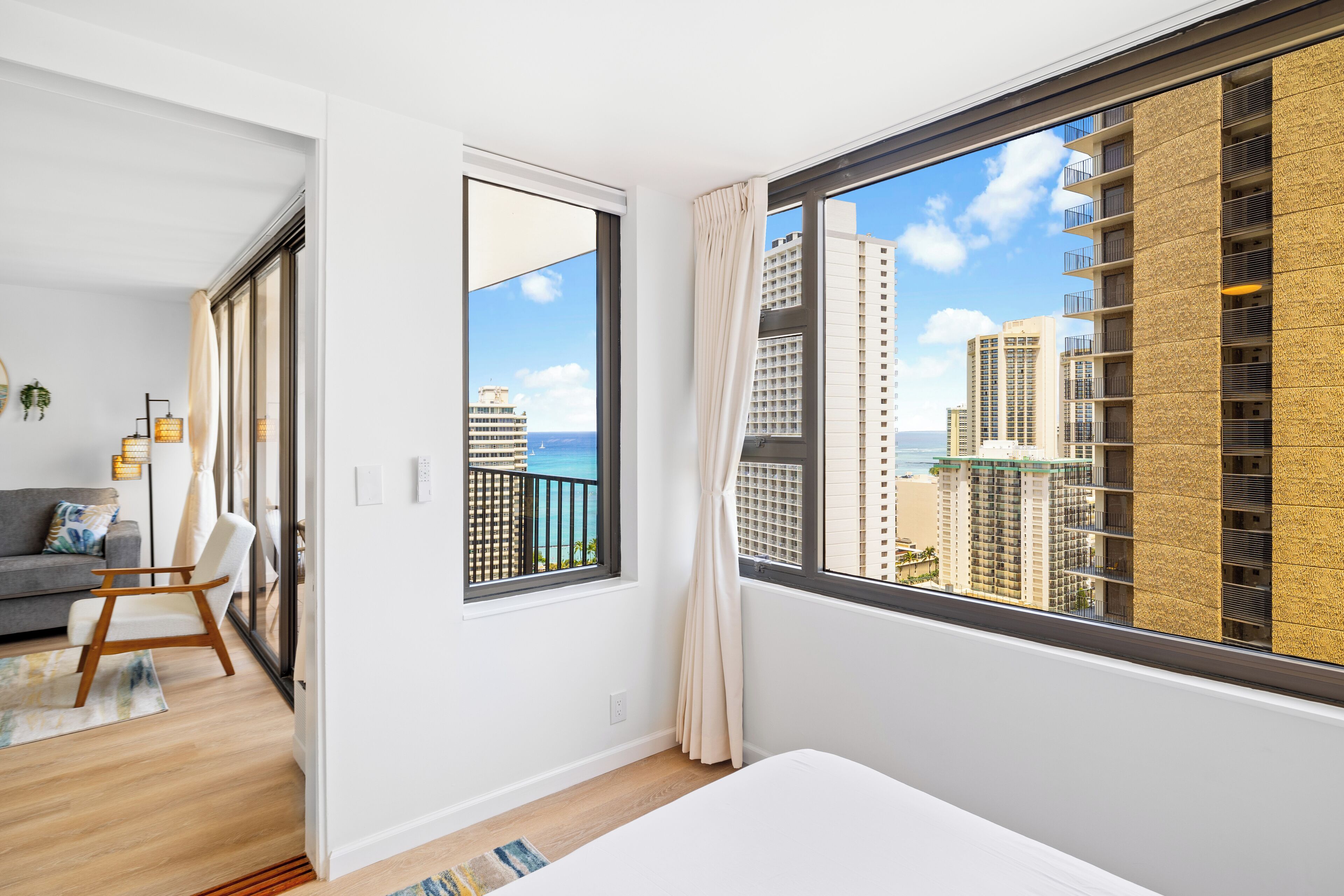 Quarto de hotel moderno com uma janela grande que oferece vista para o horizonte da cidade e para o oceano.