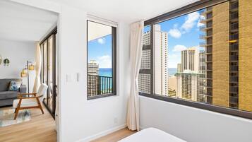 Quarto de hotel moderno com uma janela grande que oferece vista para o horizonte da cidade e para o oceano.