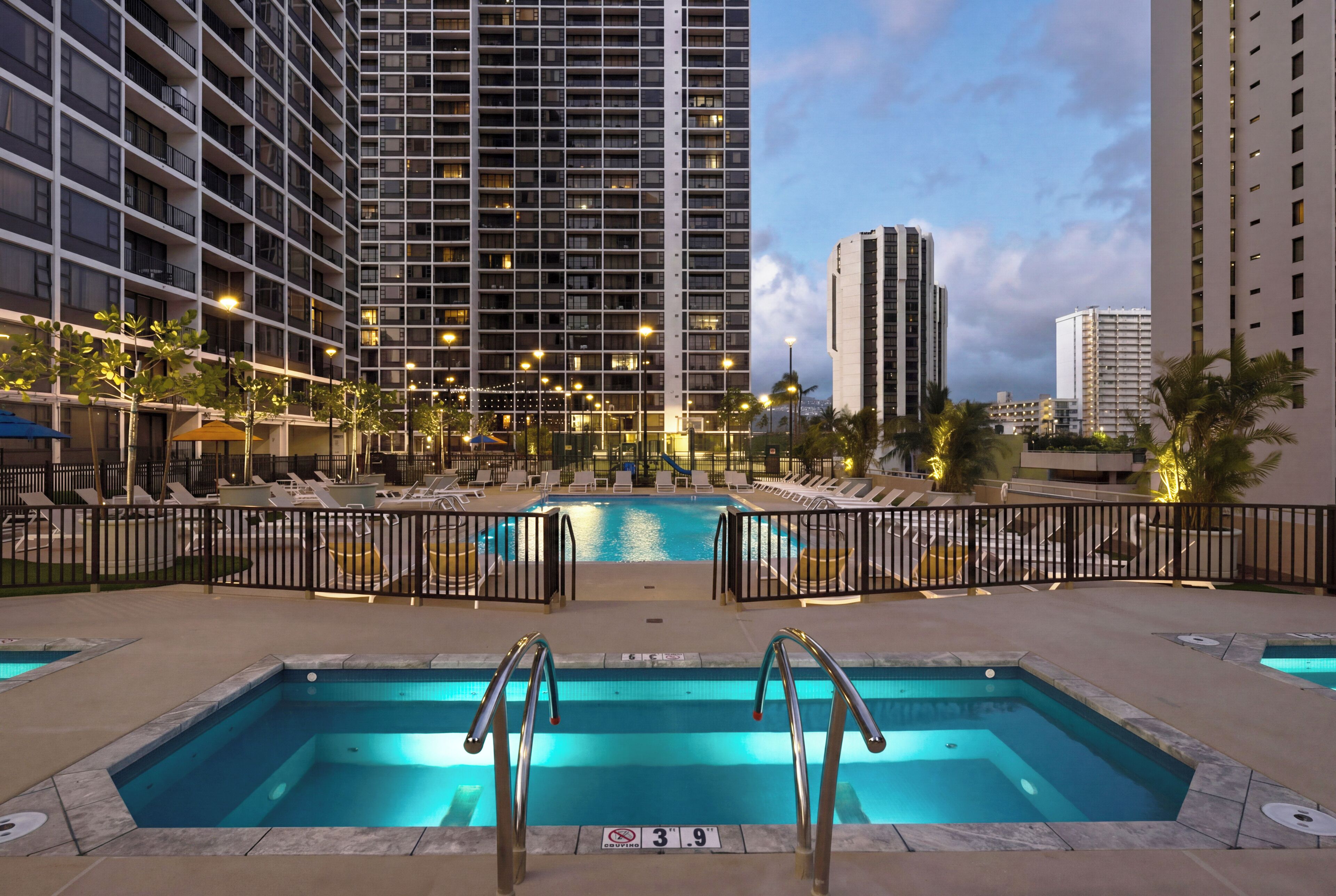 Área da piscina com vista para edifícios altos, cadeiras de descanso e placa de proibição de natação.