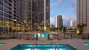 Área da piscina com vista para edifícios altos, cadeiras de descanso e placa de proibição de natação.