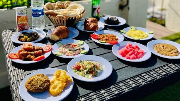Uma mesa com diversos pratos e bebidas, uma garrafa de água e uma cesta de pão em um terraço com uma pirâmide ao fundo.