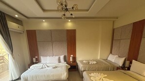 Quarto de hotel com duas camas, um ventilador de teto e uma janela grande.