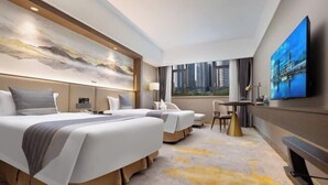 Quarto de hotel com duas camas, uma escrivaninha, uma TV e uma janela grande com vista para a cidade.